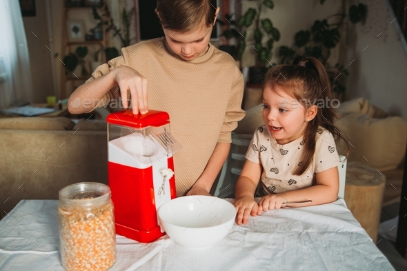 Kids cook popcorn at home in a popcorn maker. Stock Photo by vershinka_com
