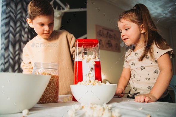 Kids cook popcorn at home in a popcorn maker. Stock Photo by vershinka_com