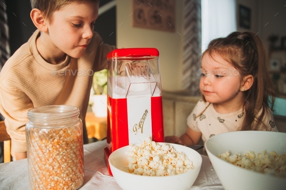 Kids cook popcorn at home in a popcorn maker. Stock Photo by vershinka_com