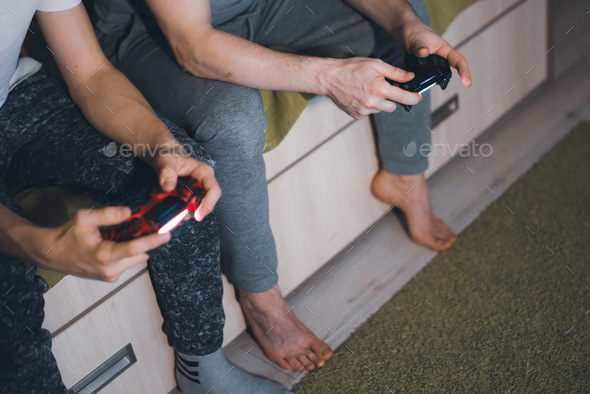 The hands of two men with joysticks who play a console at home in the ...
