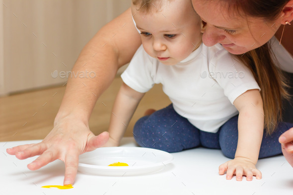 Mom and baby draw on a sheet of Whatman with their fingers in yellow ...