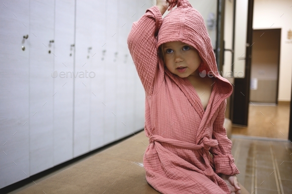little girl after class in the pool sits in a dressing gown in the ...