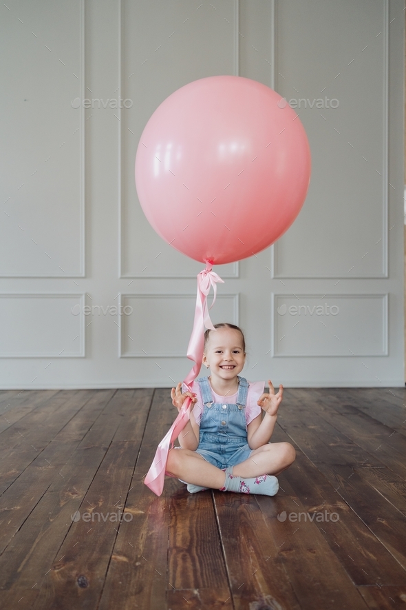 Cheerful little girl sitting in a yoga pose with a big pink balloon ...