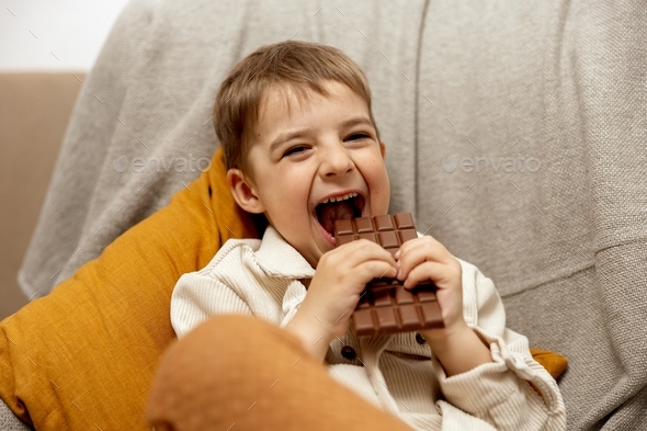 Little adorable boy sitting on the couch at home and eating chocolate ...