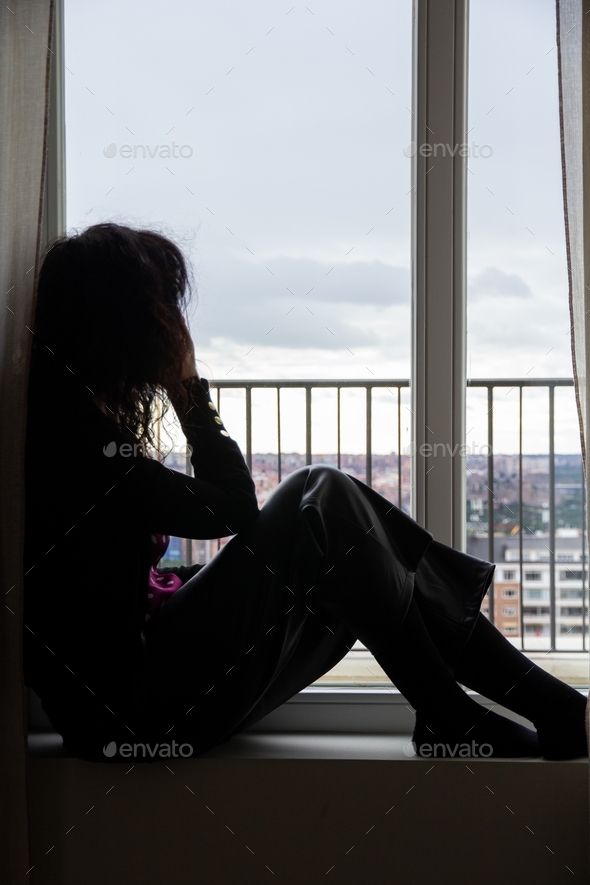 Woman in shadow sitting by the window with hand on head looking ...