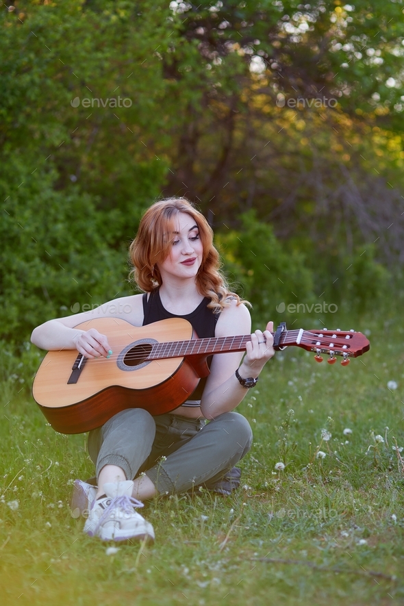 Smiling woman playing guitar around spring nature. Self-care and mental ...