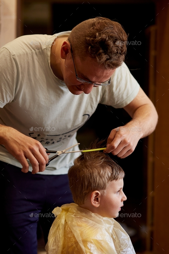 Father makes haircut to his little son with scissors and hair brush at ...