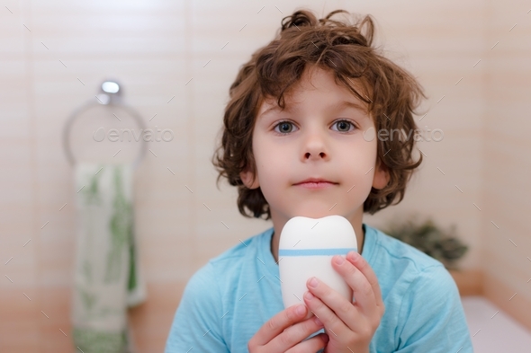 cute curly boy holds big tooth in bathroom. The concept of children's ...