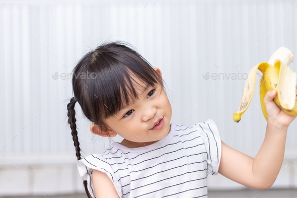 A little girl biting and eating a banana Stock Photo by kookkaibuu