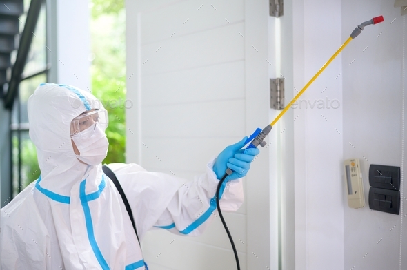 A medical staff in PPE suit is using disinfectant spray in living room ...