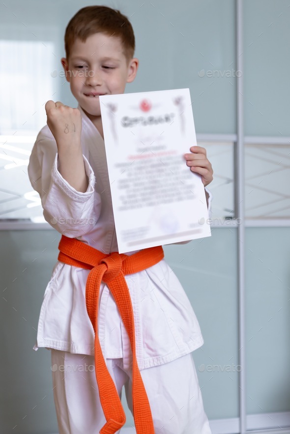 boy is awarded a karate diploma. He wears a white kimono and an orange ...