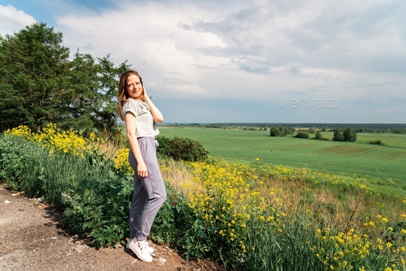 Young girl in a field with flowers. green grass. Blonde. Standing happy ...