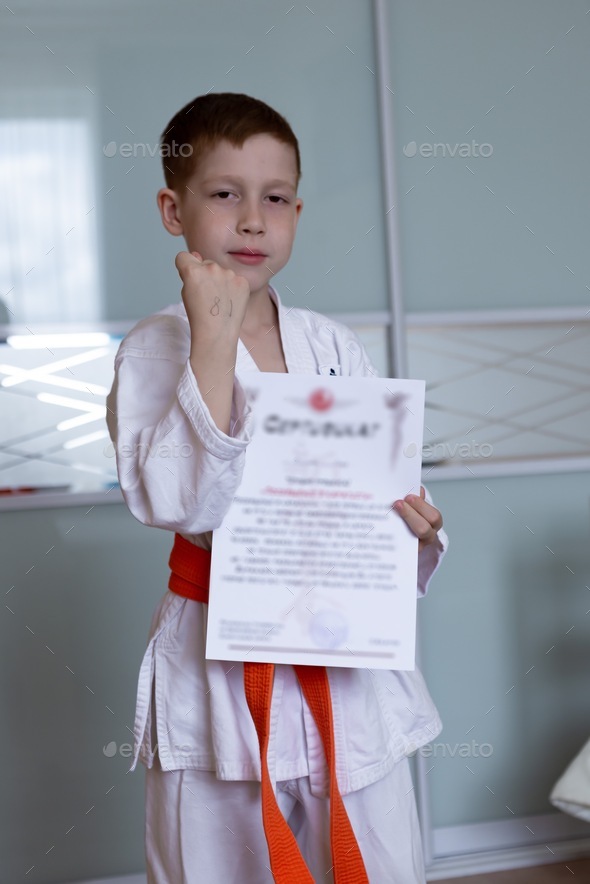 boy awarded a karate diploma. He is wearing a white kimono and an ...