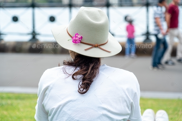 Lady from behind wearing a broad brim hat relaxing at a park in the sun ...