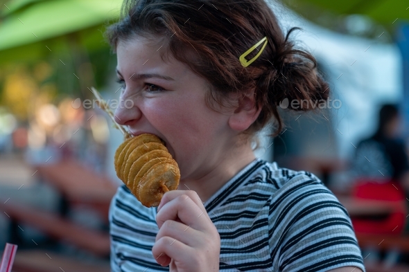 child eating potato spiral chips on a stick at a local country fair ...