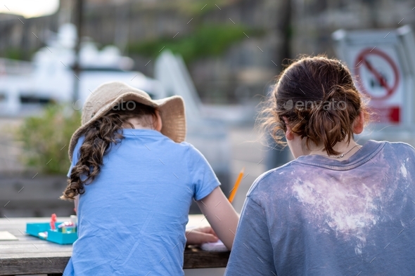 view from behind of two children sitting outdoors colouring in together ...