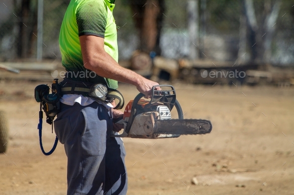 workman holding a chainsaw on a work site in work clothing, starting up ...
