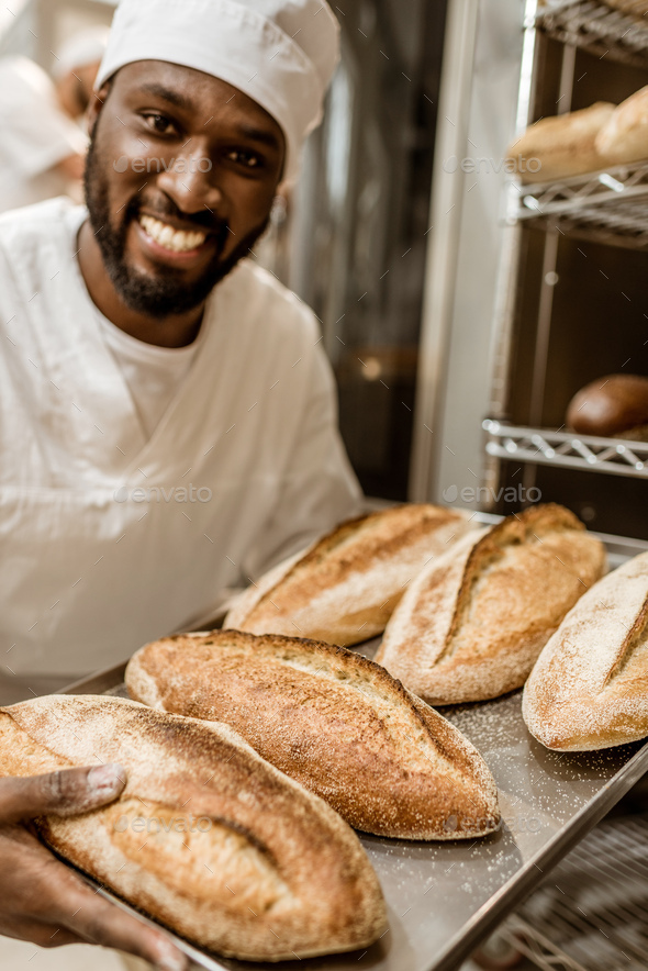 smiling handsome african american baker with tray of fresh loaves of ...