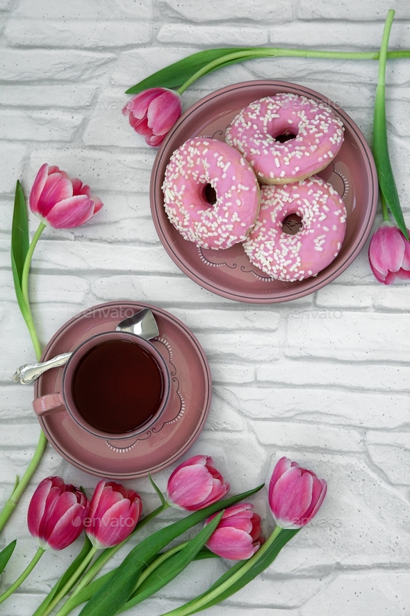 Spring layout with pink tulips, a cup of tea and pink donuts on a light ...