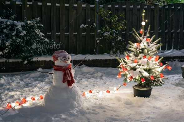 Christmas tree and snowman stand in a snowy backyard at night. Stock ...