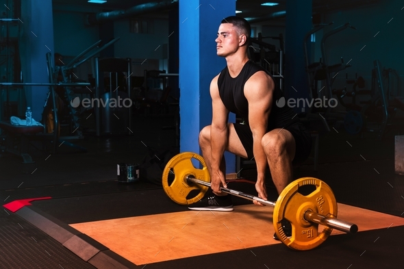 A young man lifts a barbell. Correct body position when lifting weights ...