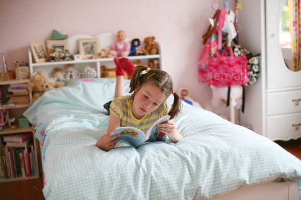 Tween girl with pony tails reading a book on her bed in her room Stock ...
