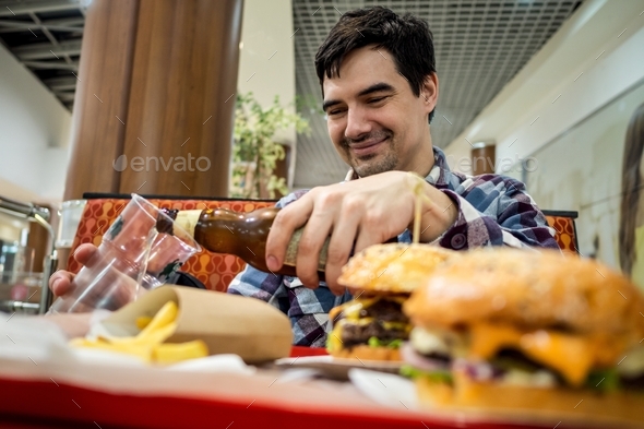man eating burger fast food and drinking beer alone in the open area ...