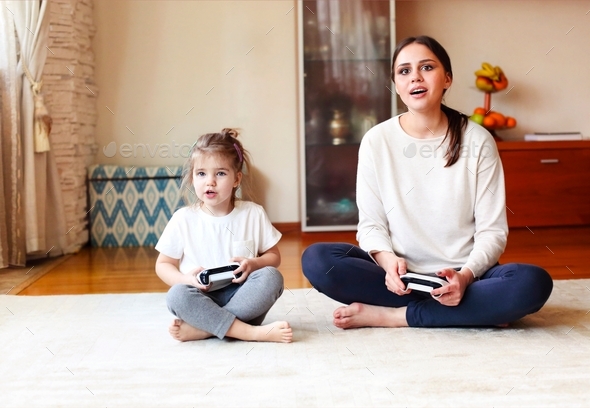 Delighted woman and girl with gamepads smiling while sitting cross ...