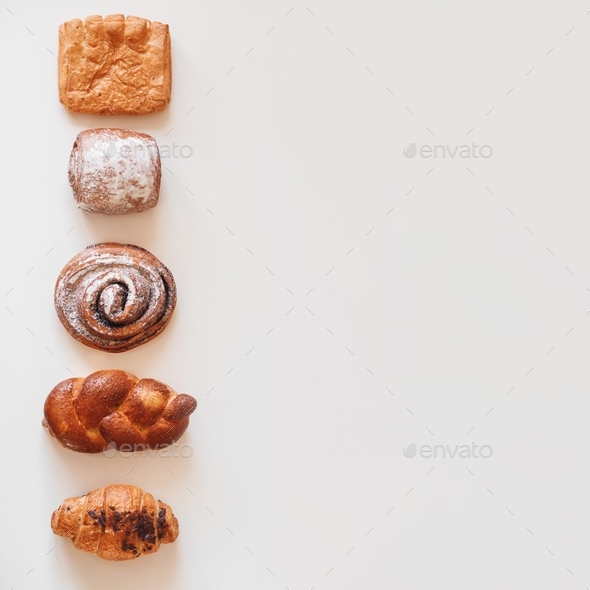 Various types of yeast and puff pastry buns laid out in row on white ...