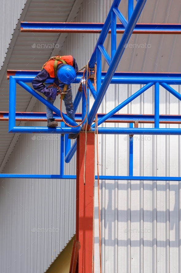 Welder with safety equipment welding metal roof structure of warehouse ...