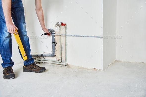 Plumber checks pipe vertical level after installation. Man with level ...