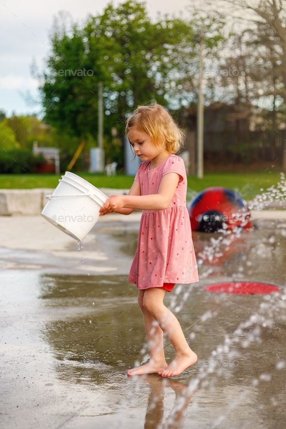 Child playing with bucket at splash pad playground in water park. Girl ...