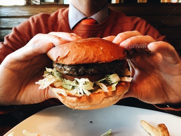 Front on shot of a delicious burger held with two hands by a man in an ...