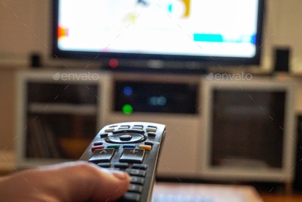 A hand holding a remote control aiming it at a television trying to ...