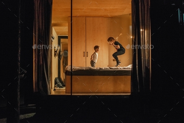 In the window of the house, a little girl and a boy jump on the bed ...