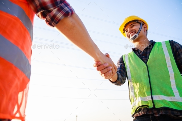 Two engineers shaking hands in construction site at the sunset ...