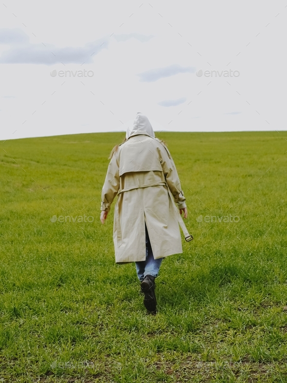Lonely girl walking into the distance across a green field Stock Photo ...