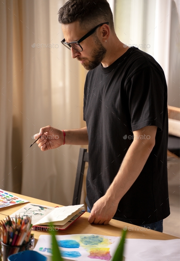 Portrait of concentrated male artist standing near a table drawing in a ...