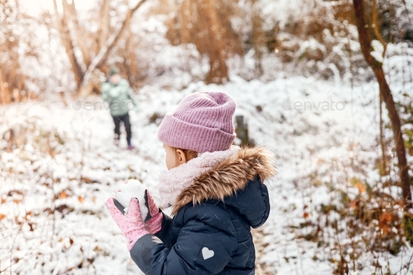Two sisters playing snowball fight in forest under falling snow sunny ...