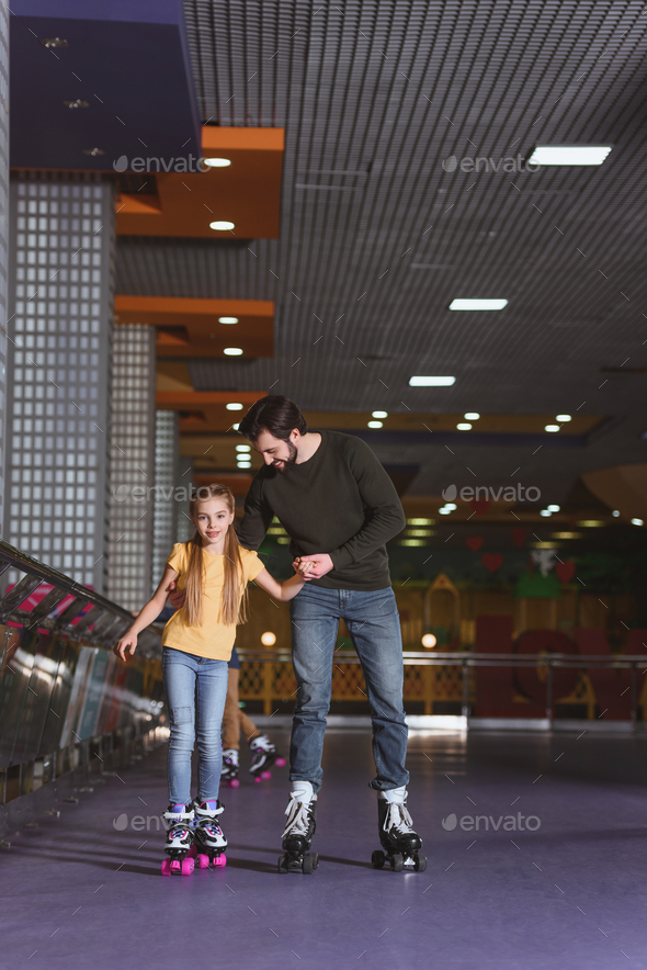 father and daughter holding hands while skating together on roller rink ...