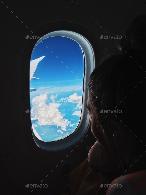 Silhouette of woman looking out of airplane window during flight. Blue ...