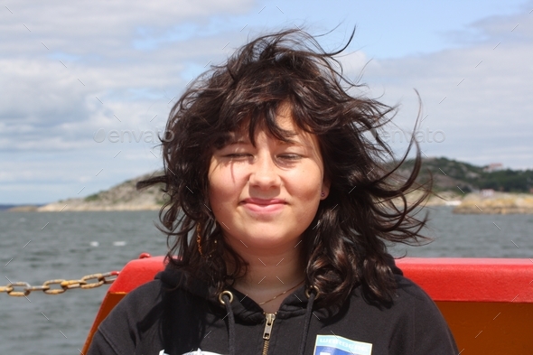 Happy teenager girl on a ferry, windy wild dark hair and sunny face ...