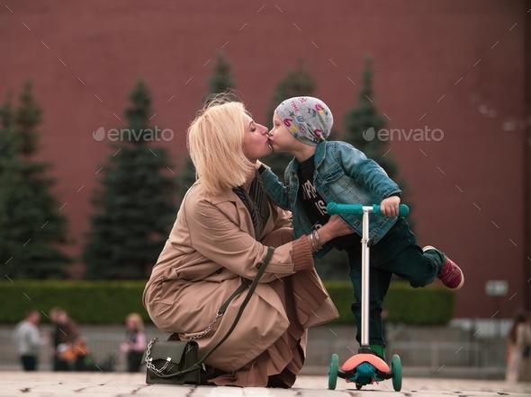Mom kisses a passing child on a scooter. Mom and son on a walk Stock ...