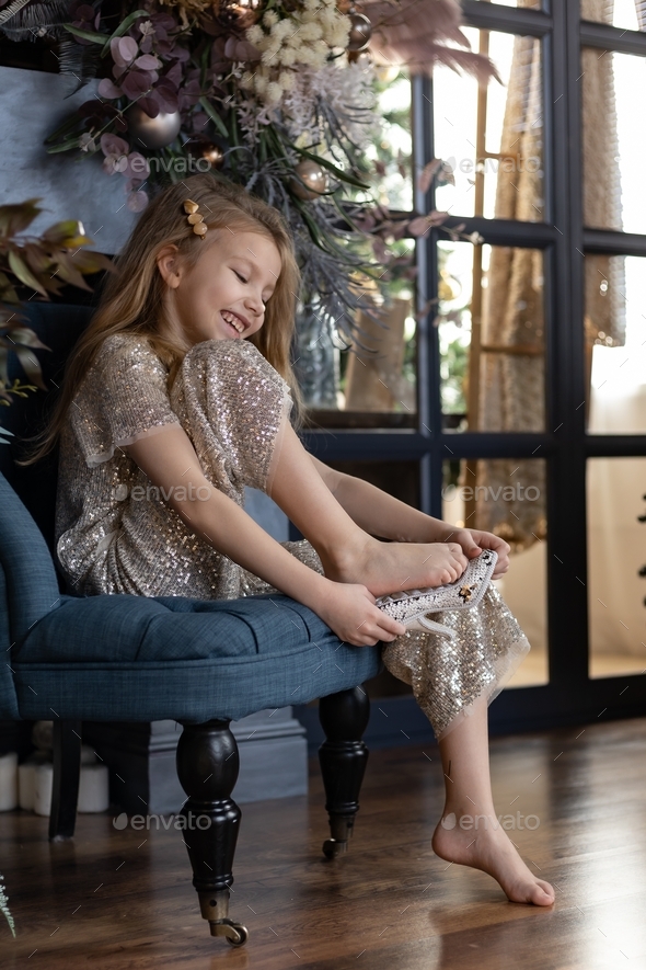 a cute six-year-old girl in a shiny suit is sitting on an easy chair ...