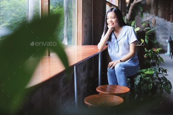 Woman sitting next to glass window looking outside through window with ...