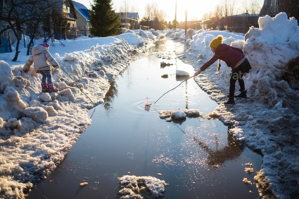 children play in puddle on street in early spring. snow melting on road ...