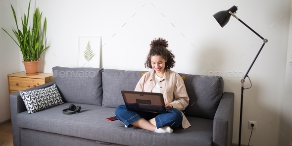 mixed rase girl is sitting on couch and looking at at computer screen ...