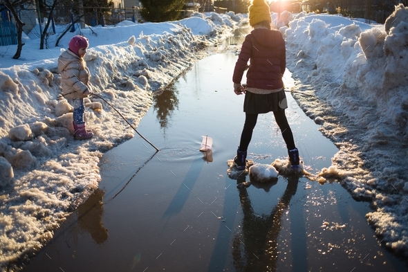 children play in puddle on street in early spring. snow melting on road ...