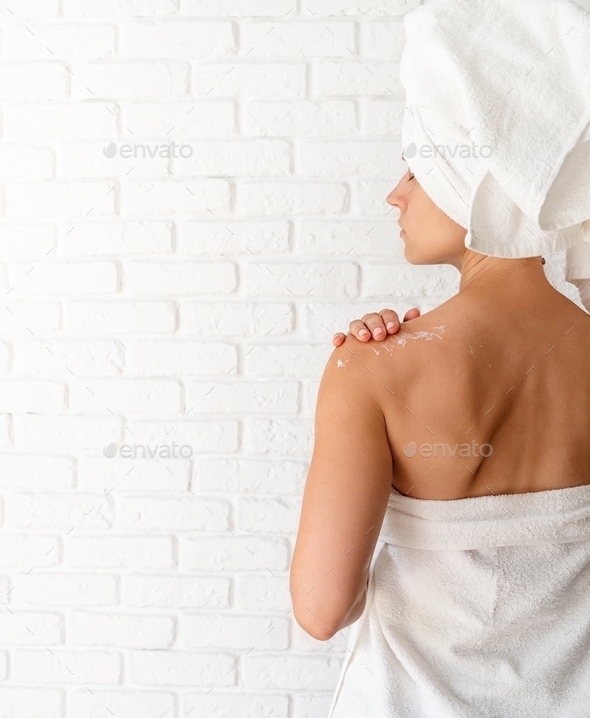 Rear view of a beautiful woman wearing white bath towels applying cream ...