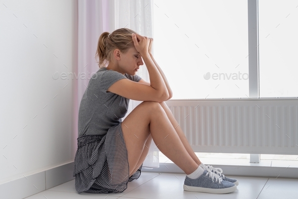 Sad woman sitting on the floor hugging her knees Stock Photo by ...